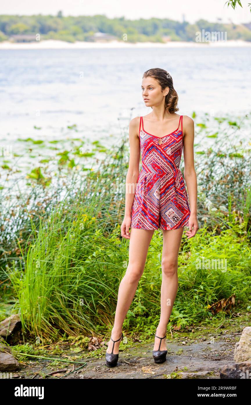 A young woman with a red dress stand close to the river's edge where ...