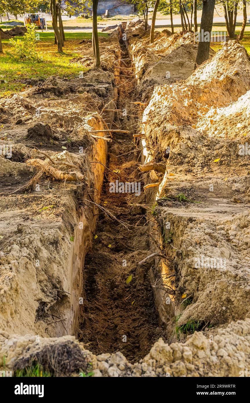 A trench in the ground for laying a pipe in the park, under the trees ...