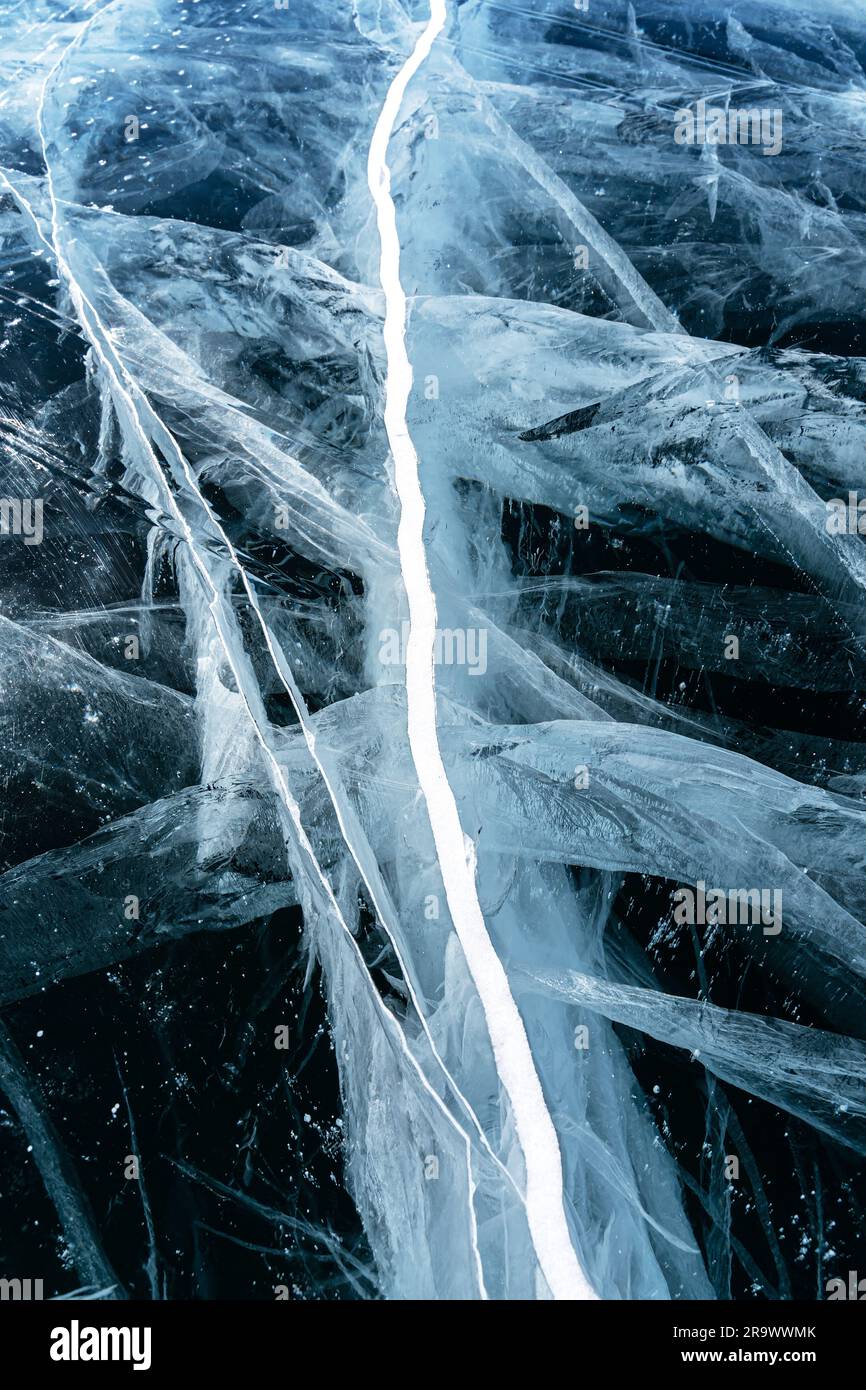 Transparent dark blue ice of frozen Baikal lake with white cracks ...