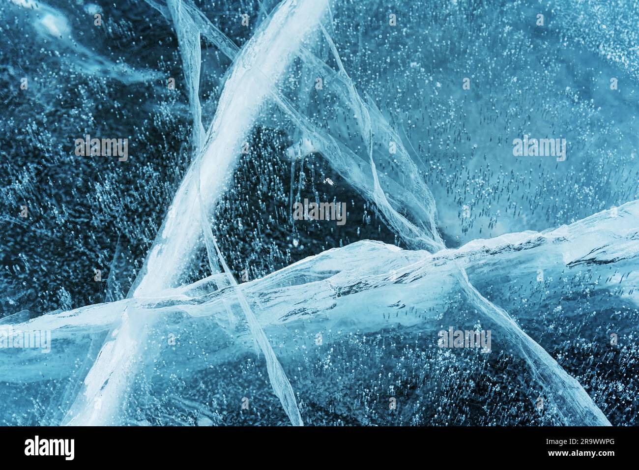 Transparent dark blue ice of frozen Baikal lake with white cracks ...