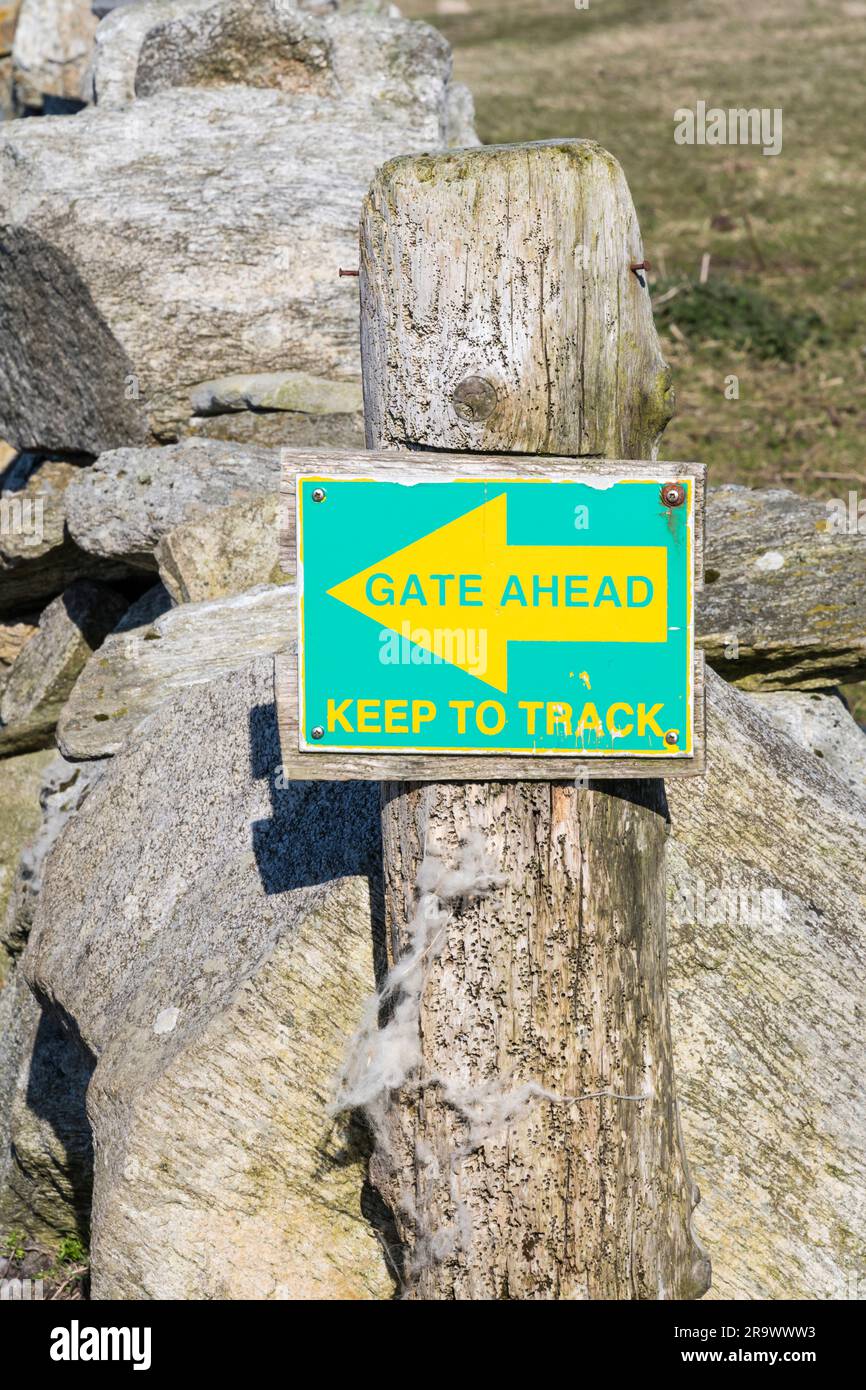 A sign reads Gate Ahead Keep to Track on a path across farmland on Yell ...