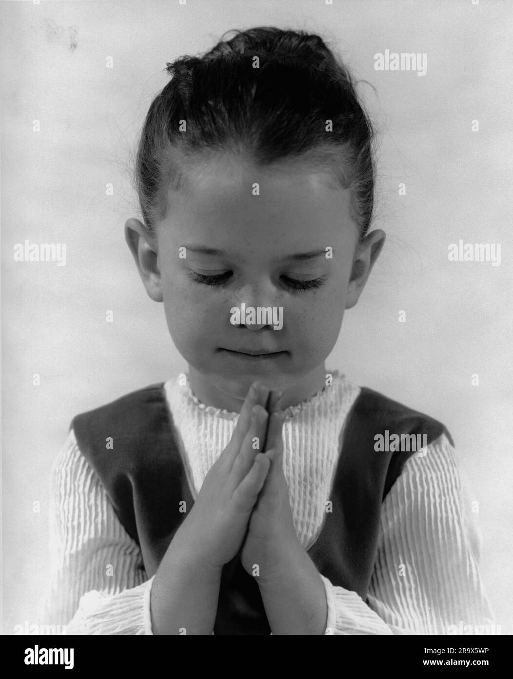 Young girl with hands clasped together praying while glancing down ...