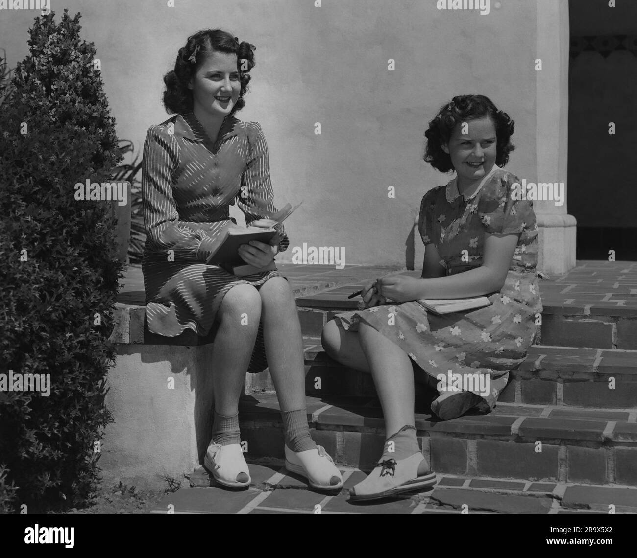 Two young college girls in dresses sitting on the steps of the school ...
