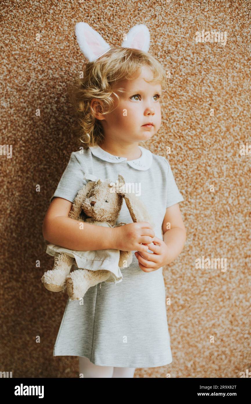 Portrait of adorable toddler girl wearing bunny ears, holding soft ...