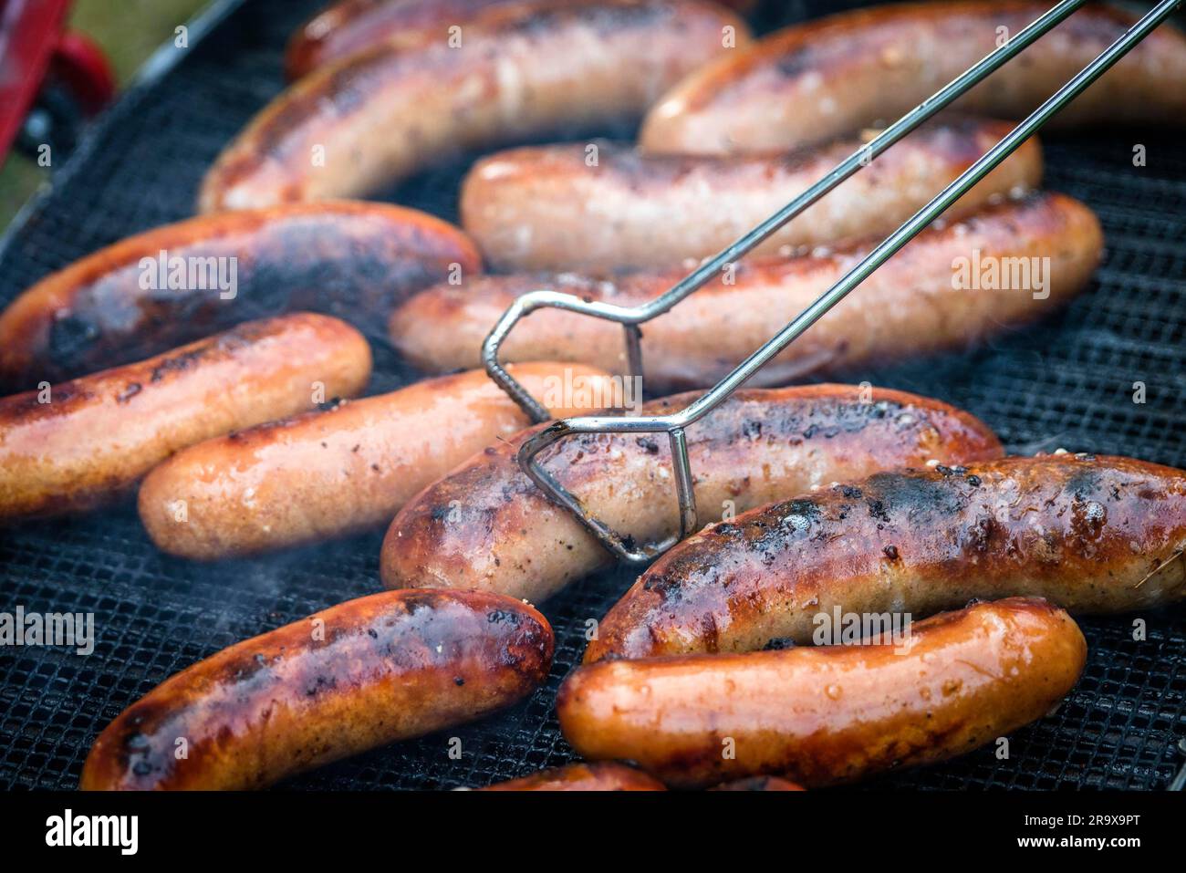Crispy wieners on an outdoor grill in the summer with a sausages plier ...