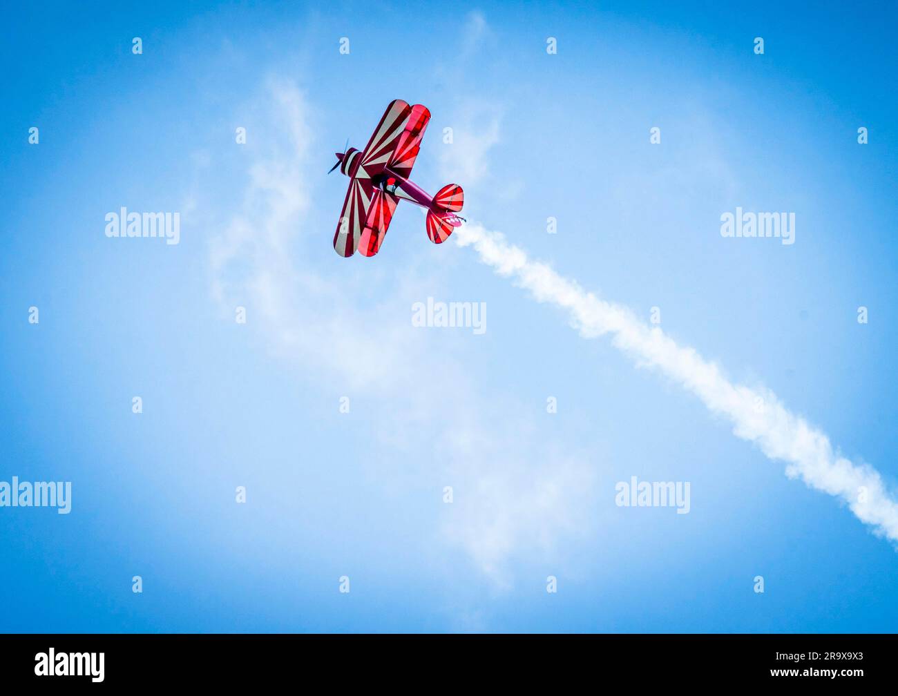 Red plane with propeller flying upward with white smoke on the tail in ...
