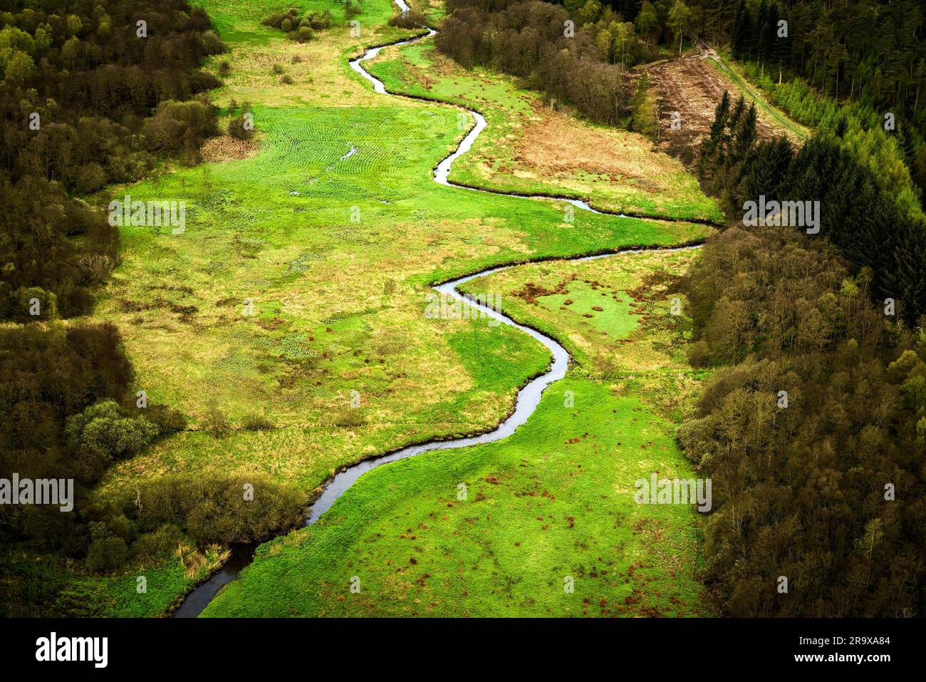 Small river going through a green area with fields and trees seen from ...