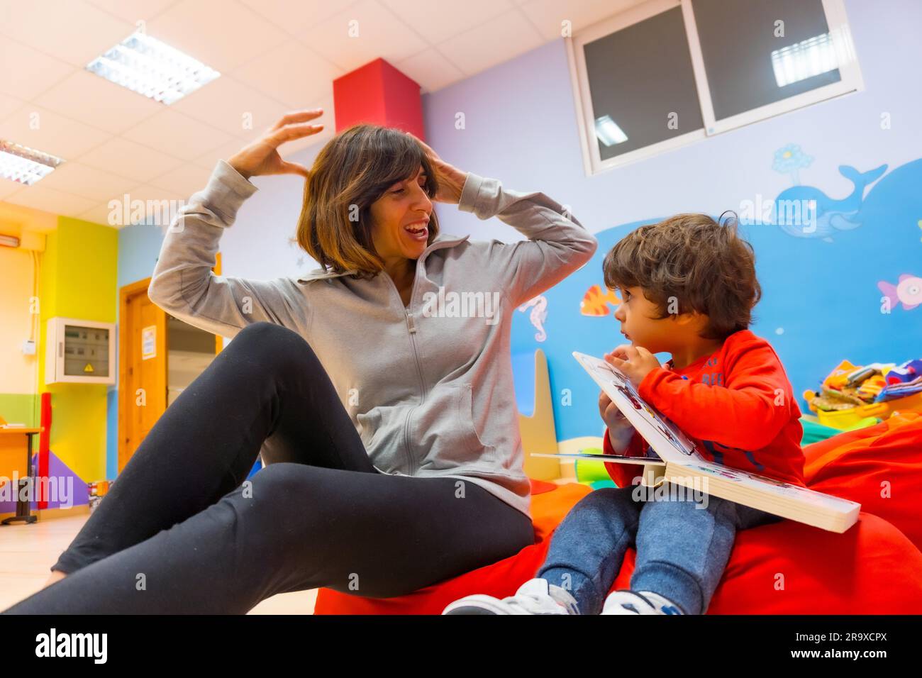 Woman teacher with a child sitting reading a book and expressing things ...
