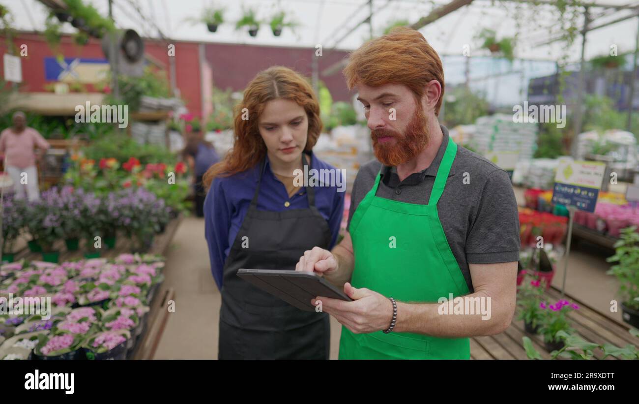 Two employees looking at tablet device standing inside Flower Shop. A ...