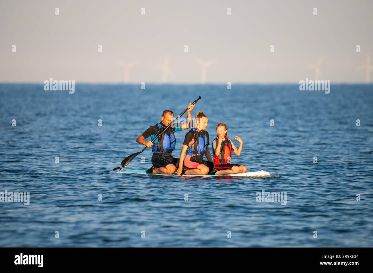 Adult male with 2 younger females (possibly a family) on a paddleboard ...