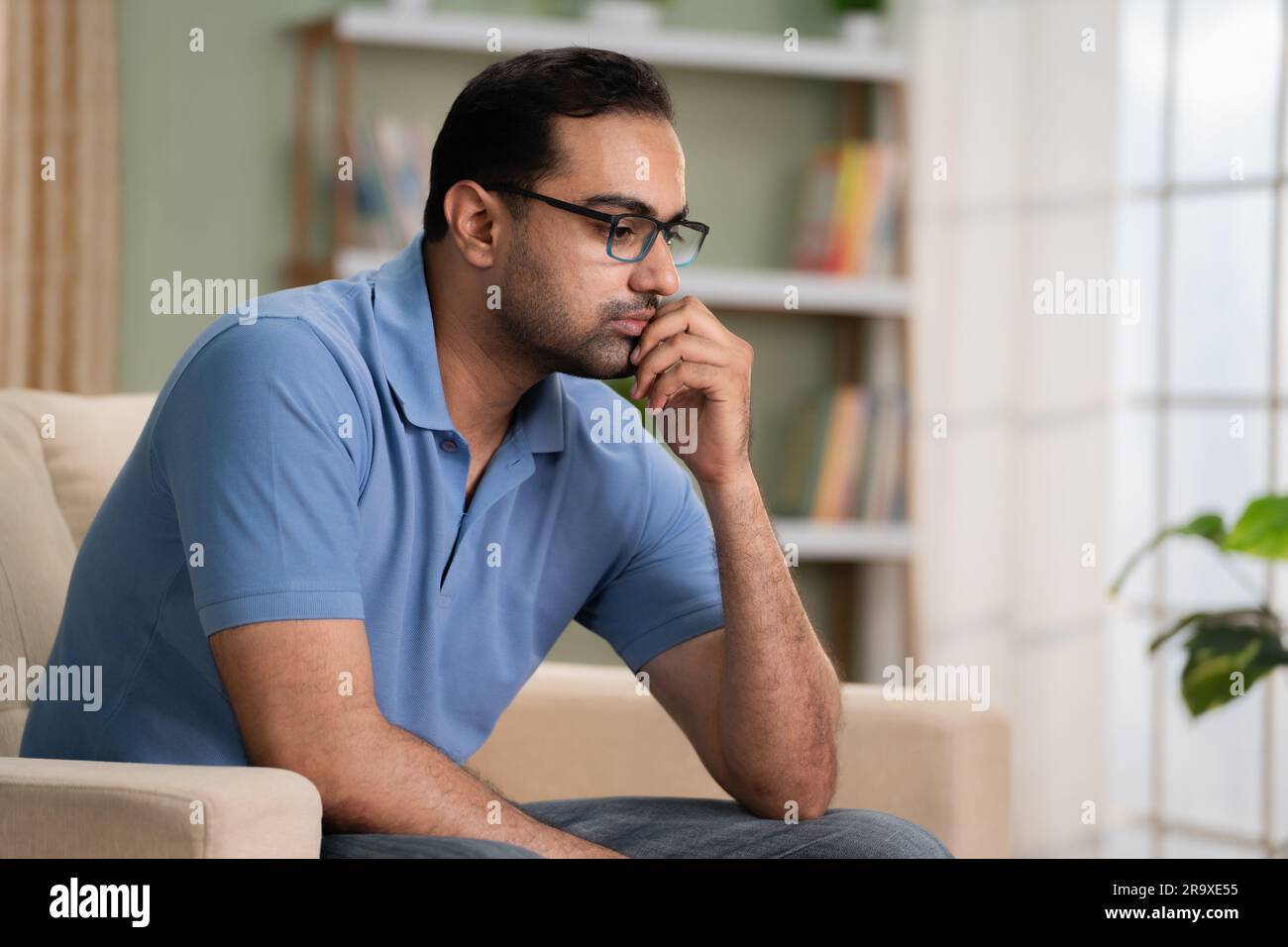 Worried indian man in deep thinking while sitting on sofa at home ...