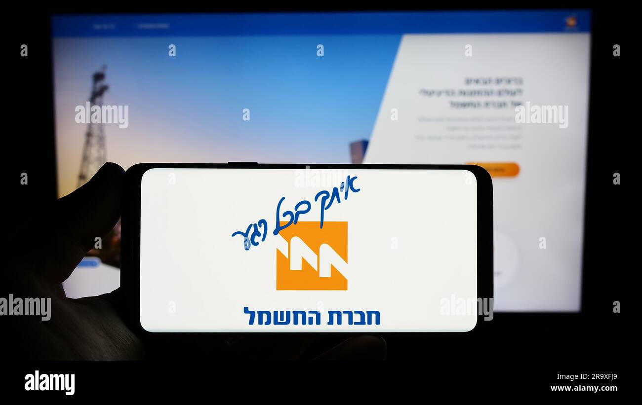 Person holding smartphone with logo of utility company Israel Electric ...