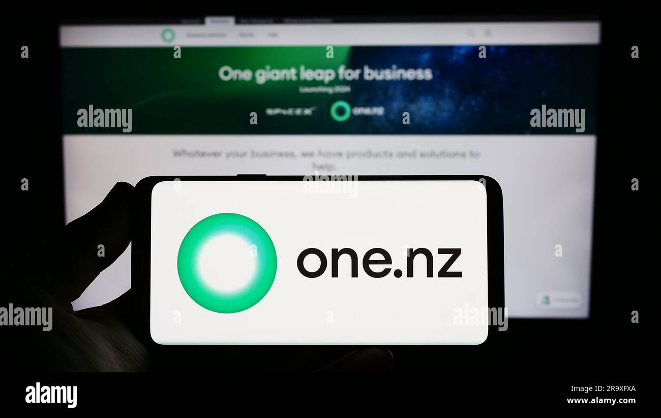 Person holding smartphone with logo of company One New Zealand Group Limited (One NZ) on screen ...