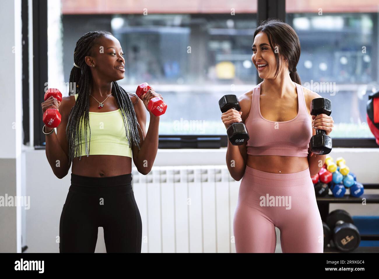 two fitness women talking to each other and working out with weights at ...
