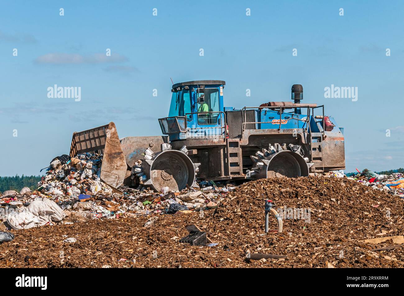 A soil compactor moving around and manipulating trash in the dirt on a ...
