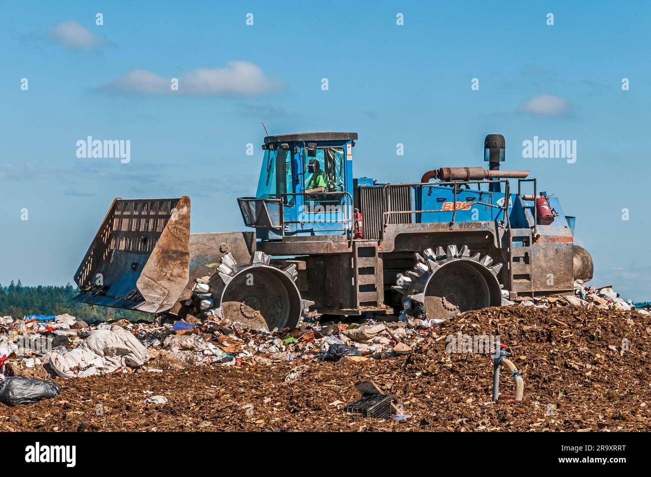 A soil compactor moving around and manipulating trash in the dirt on a ...