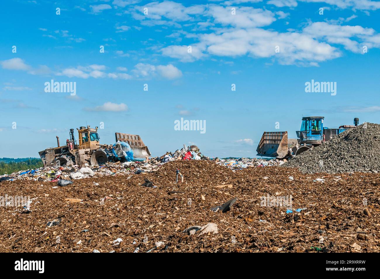A soil compactor and a bulldozer work the land in an active landfill ...