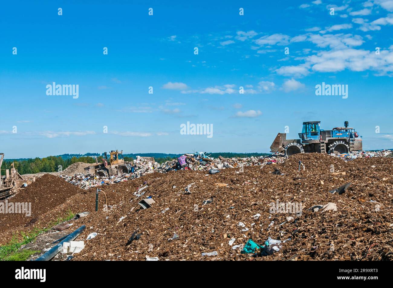 A soil compactor and a bulldozer work the land in an active landfill ...