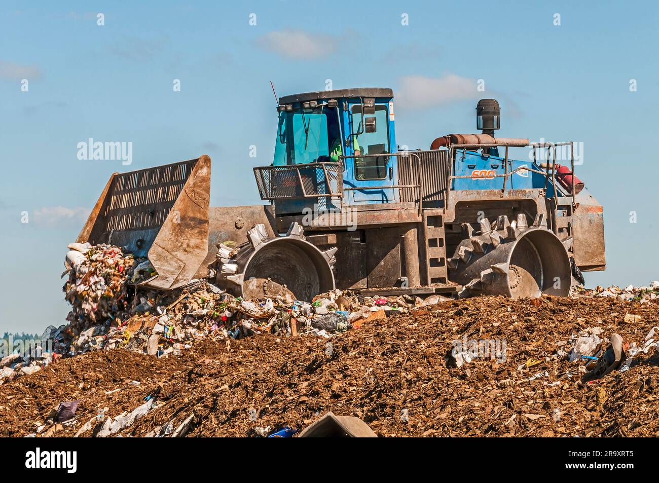 A soil compactor moving around and manipulating trash in the dirt on a ...