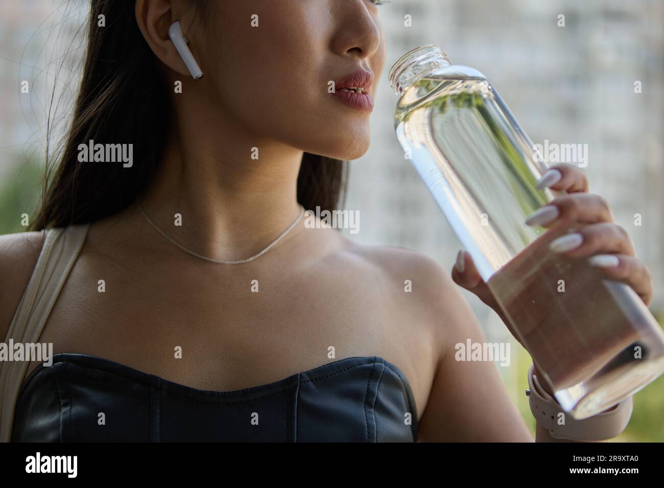 Beautiful Asian woman drinking fresh water from a glass bottle. Thirsty Vietnamese female person ...