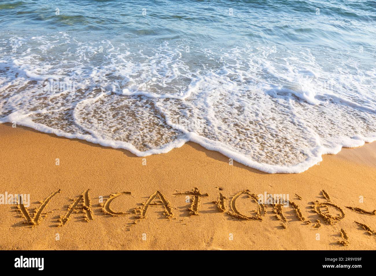 Wave washing up onto a sandy beach with Vacation handwritten ...