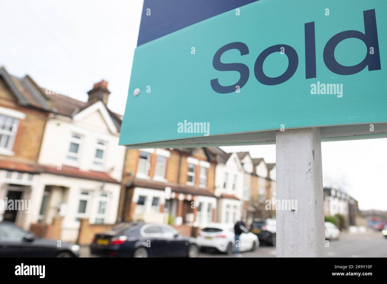 Estate agent SOLD sign with defocussed street of houses in background ...