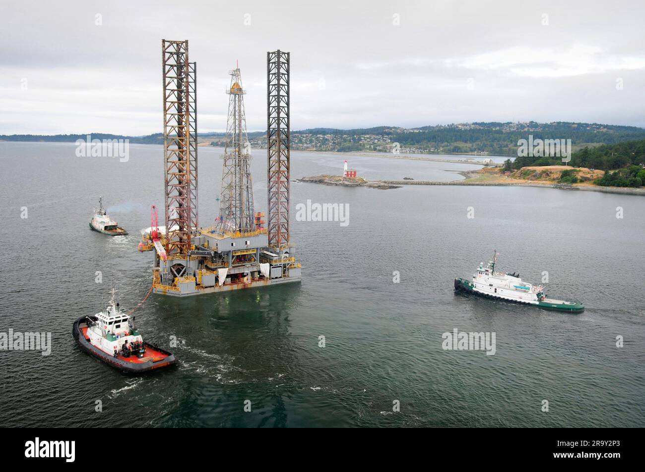 Aerial image of an oil drilling rig being towed out of port by three ...