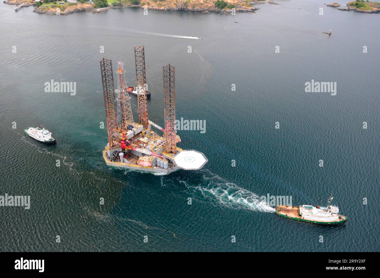 Aerial image of an oil drilling rig being towed out of port by three ...