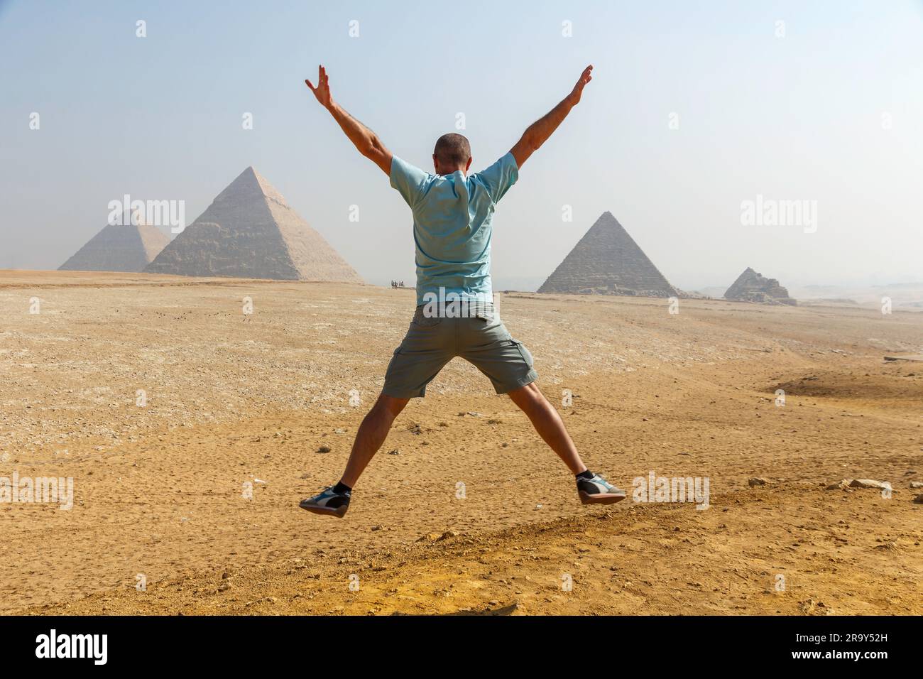 A rear view of a man jumping against the famous pyramids of Giza in ...