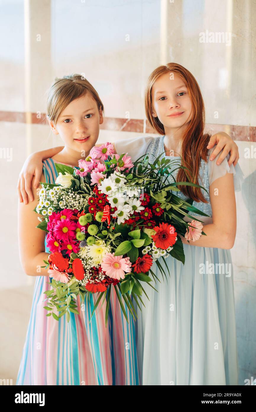 Two beautiful girls wearing occasion dresses, holding big flower ...