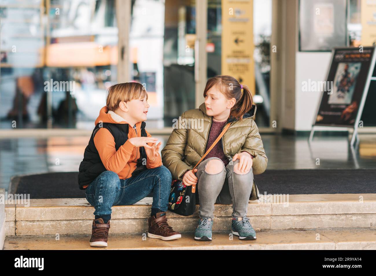 Group of two funny kids sitting on stairs next to cinema, having ...