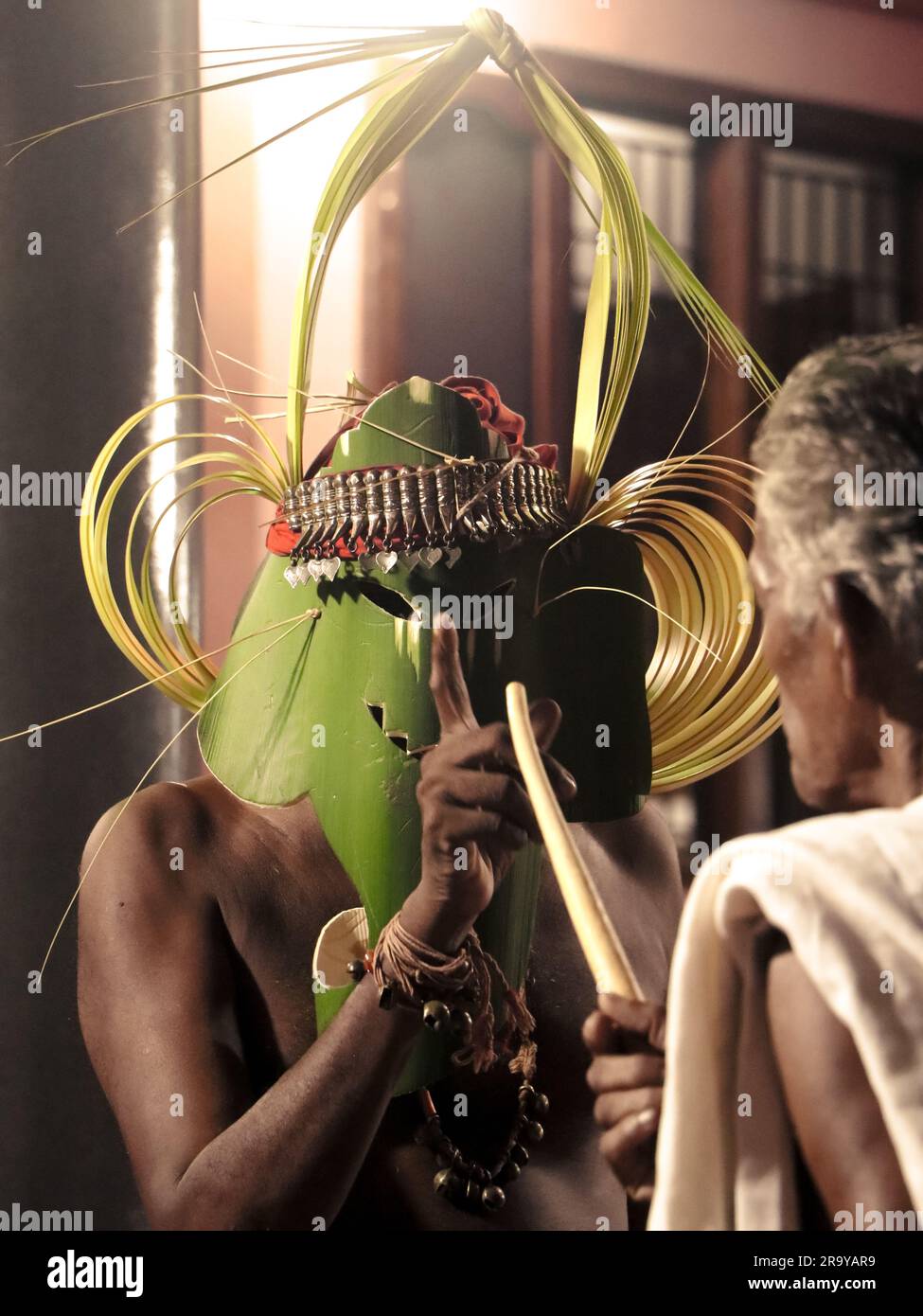 a traditional theyyam artist in a green mask having a conversation as ...