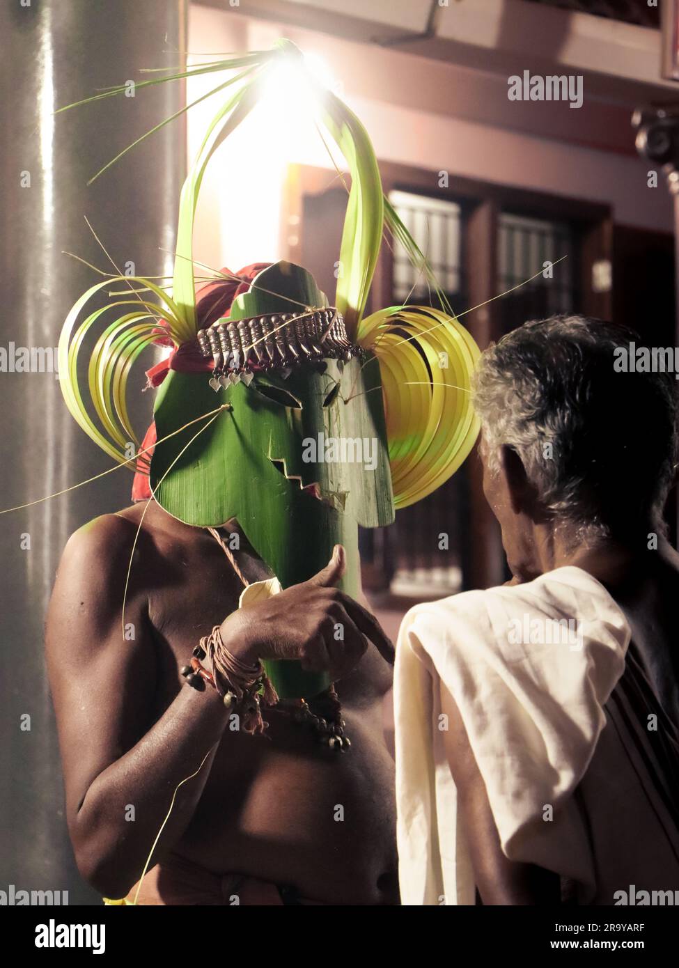 a traditional theyyam artist in a green mask having a conversation as ...