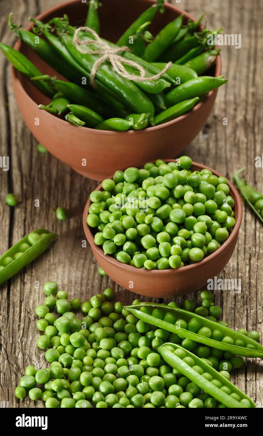 Green pea pods and peeled fresh peas in ceramic bowls, scattered green ...
