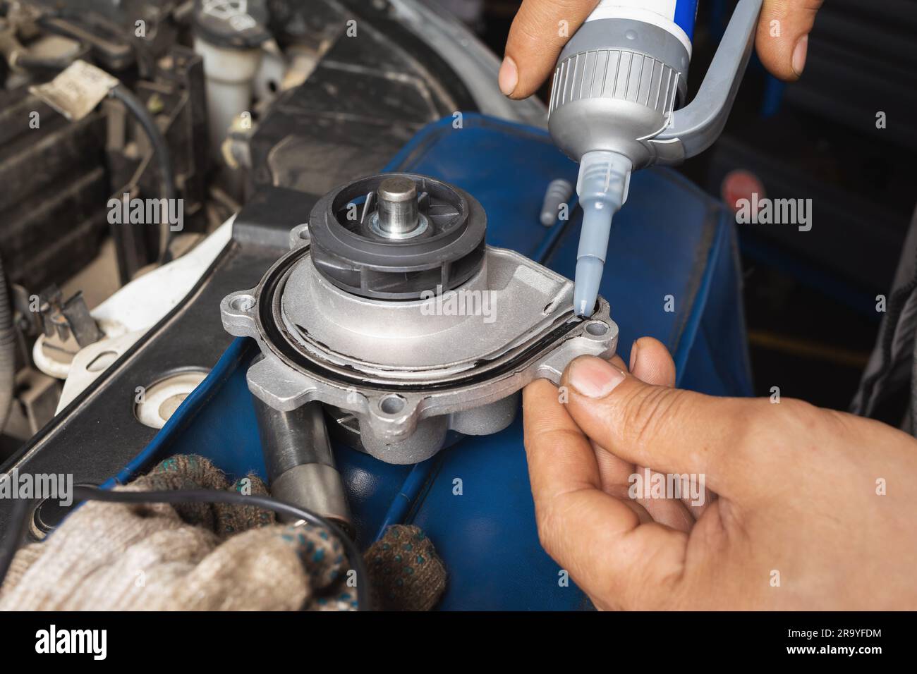 An auto mechanic applies silicone black sealant to a new engine cooling ...