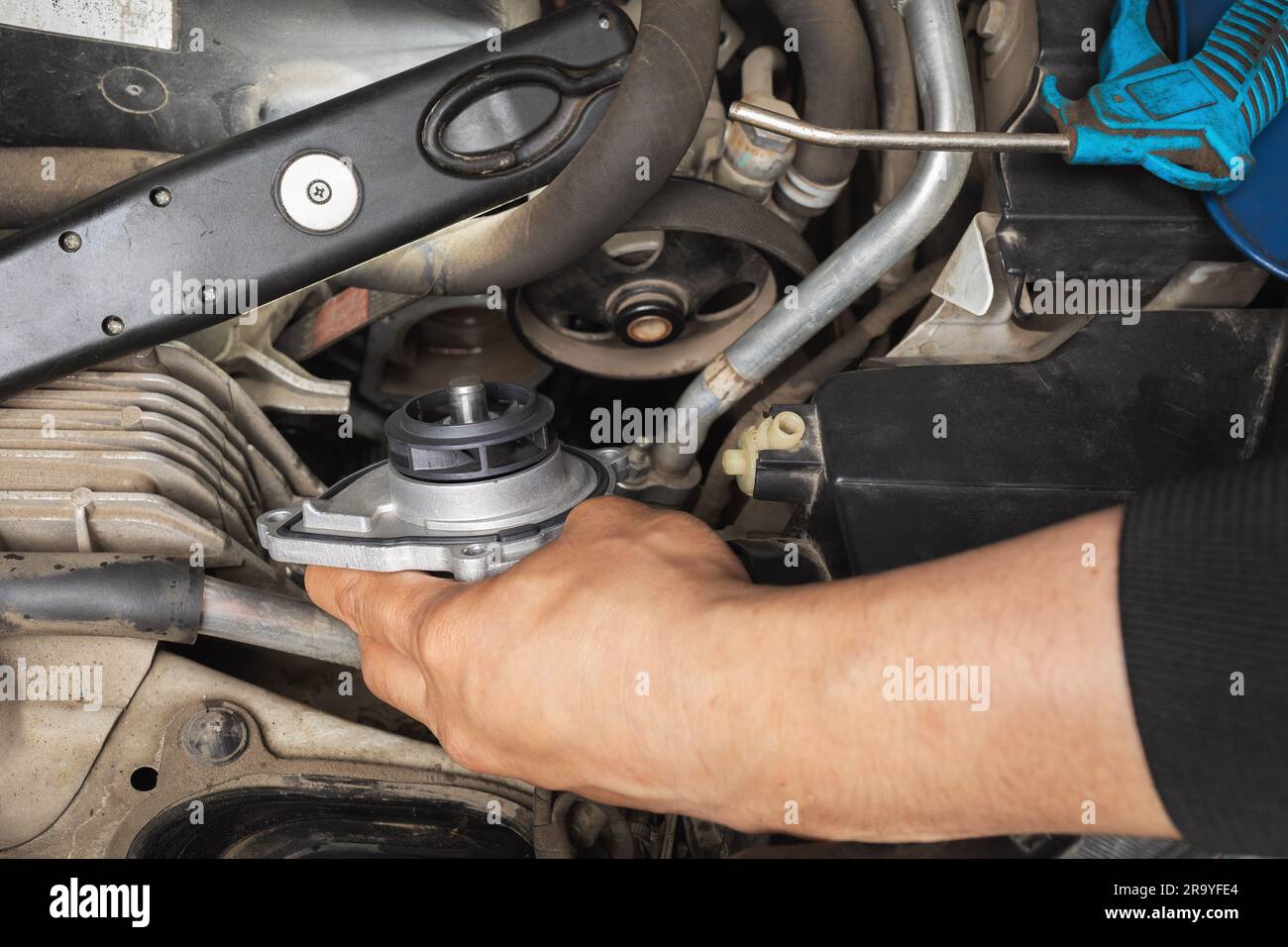 Auto mechanic installing a new engine cooling pump in a car at a ...