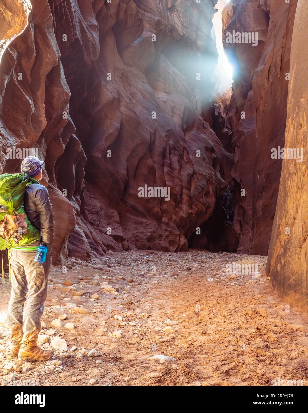 A hiker man, standing, looking at the light coming through a narrow ...