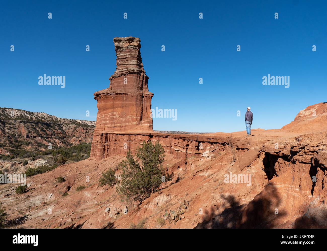 Man, person, standing on a flat plateau of watching a large rock tower ...