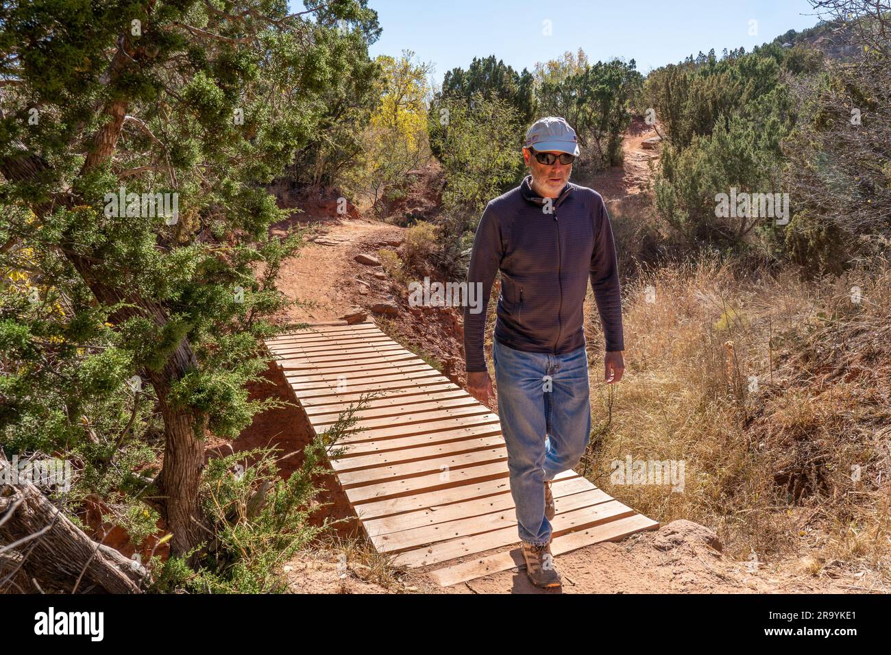 Mature Caucasian man walking across a dry stream on a wooden plank ...