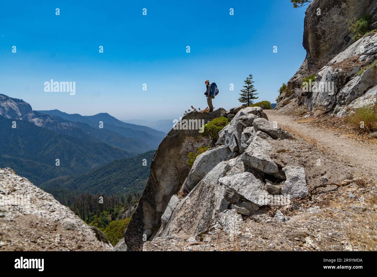 A Hiker standing on the edge of a cliff by a trail, high above a valley ...