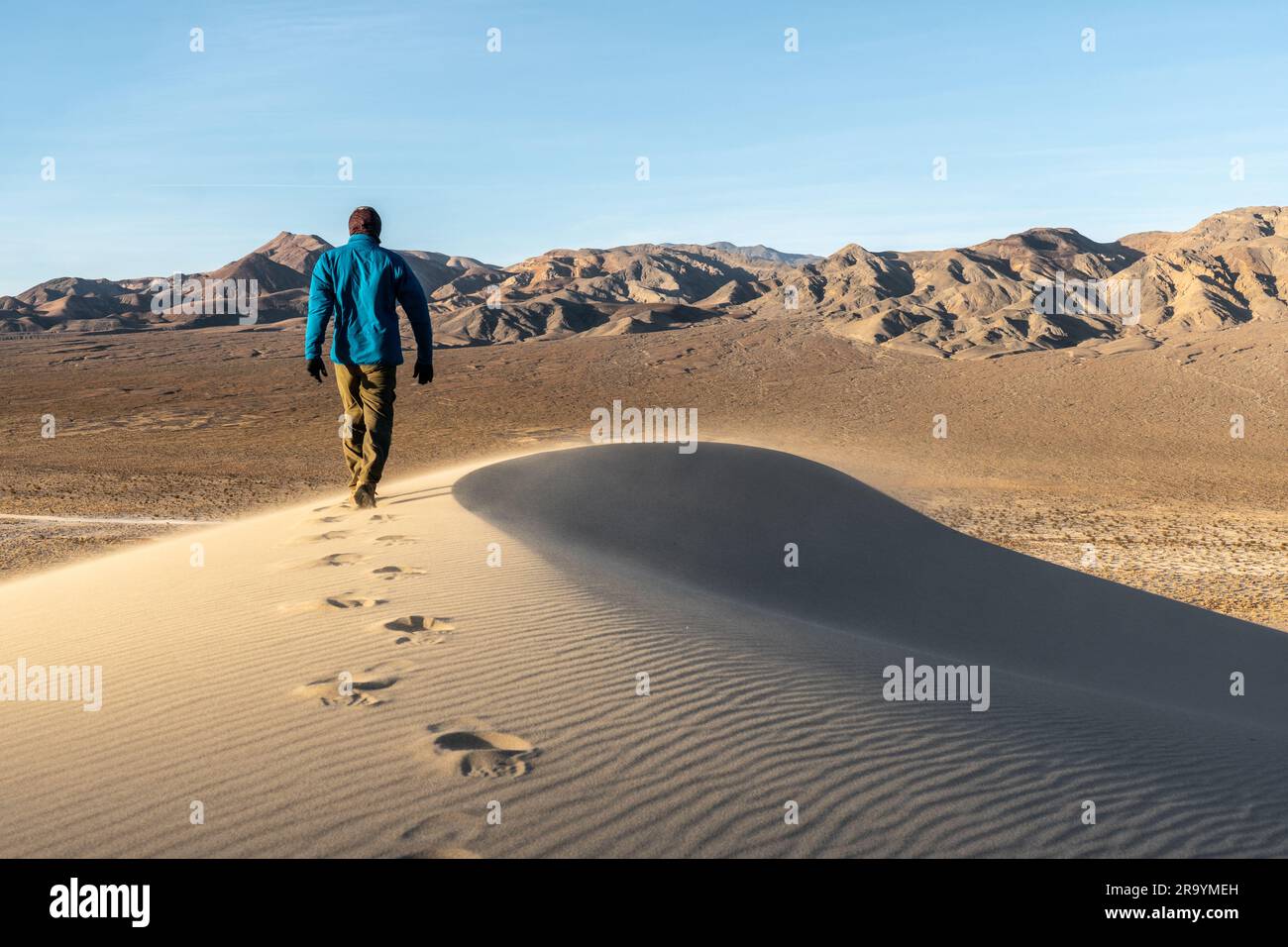 A hiker person man hiking on a sand dune leaving a track as he goes ...