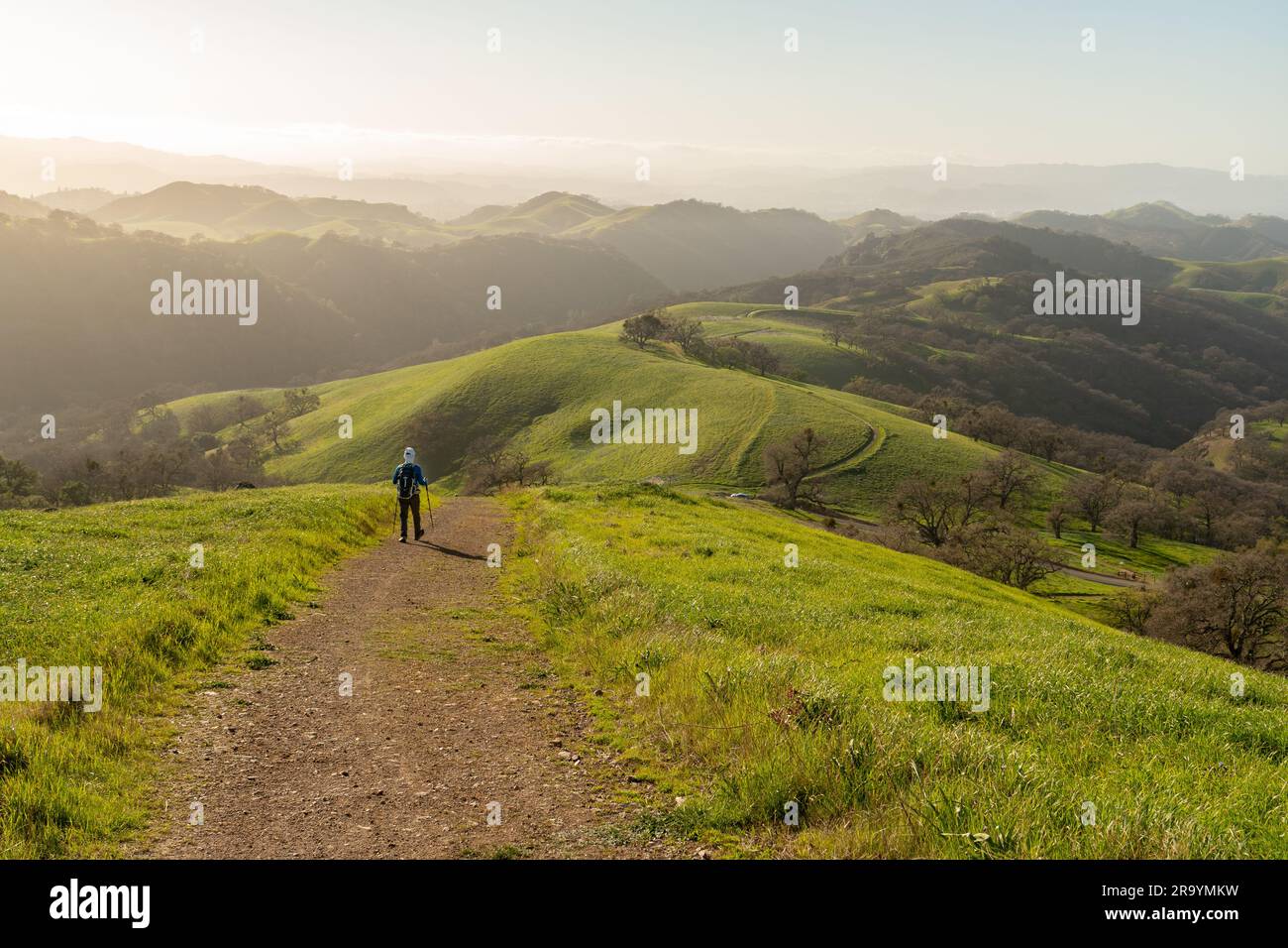 Lone hiker on a trail along a descending ridgeline with distance hills ...