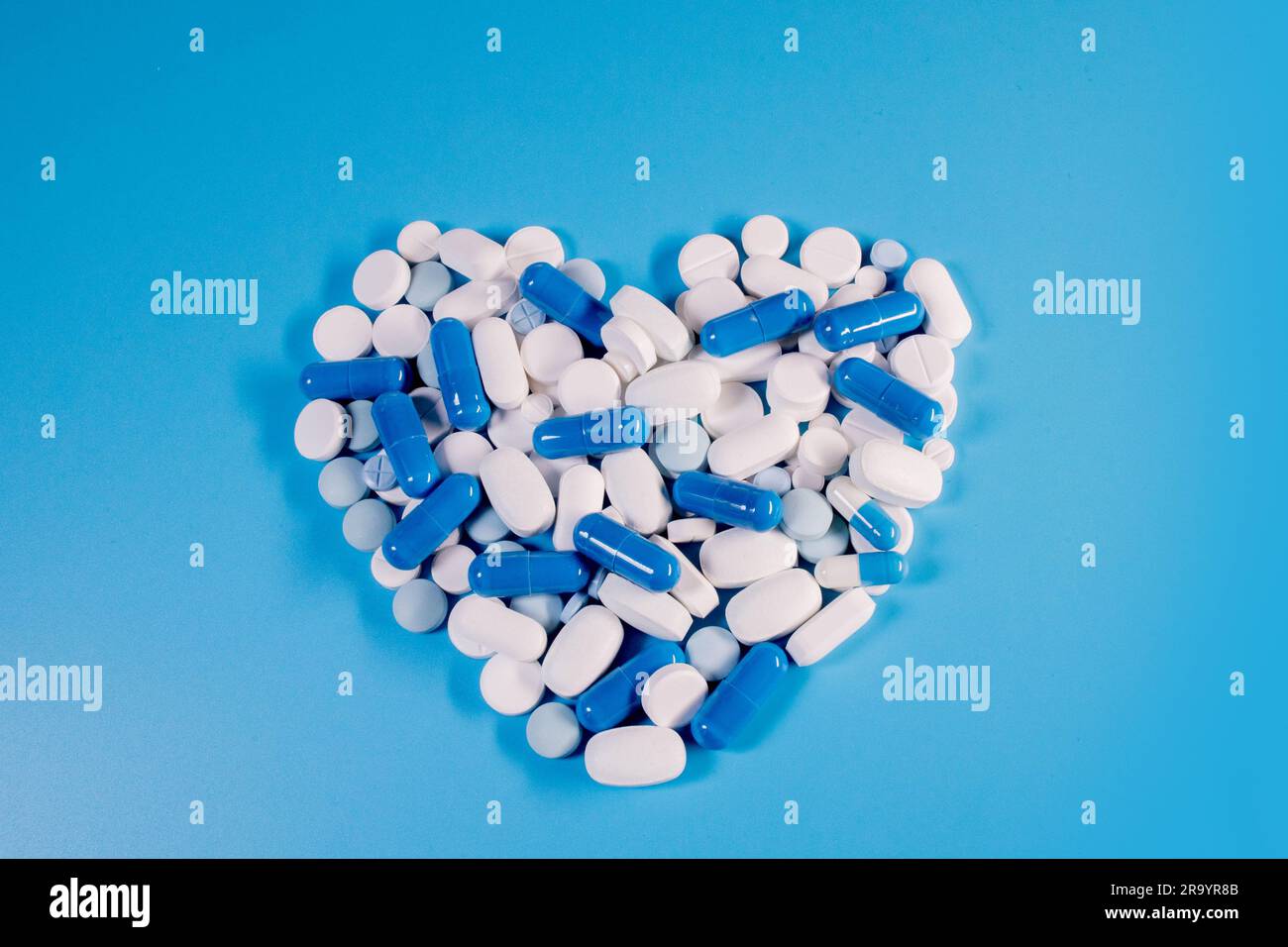 White pills and blue capsules in the shape of a heart on a blue ...