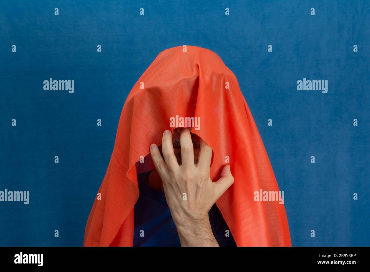 Man completely covering his head with an orange cloth and with one hand ...