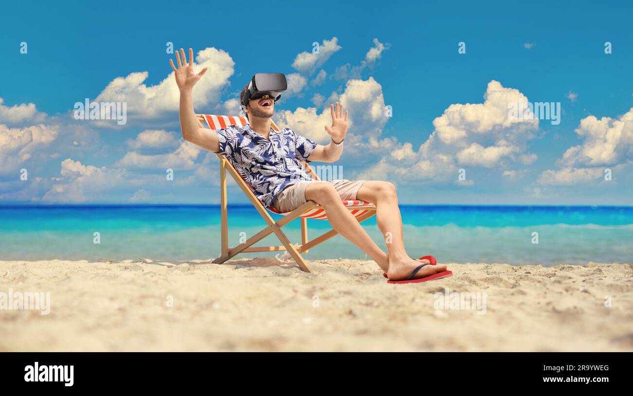 Man at the beach wearing a VR headset and sitting on a deck chair by ...