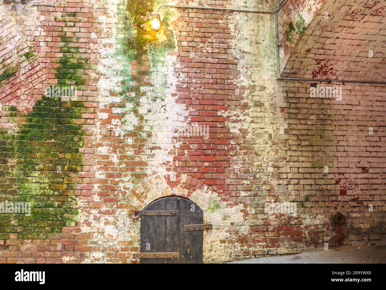 ancient mossy brick wall with black door and light. Ruinous wall wreck ...