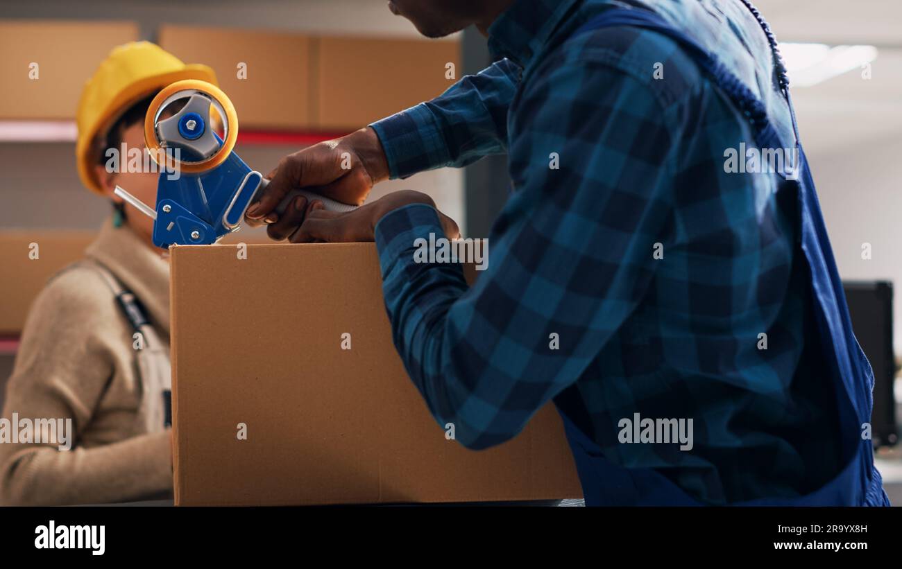 African american man putting adhesive tape on boxes, preparing order ...