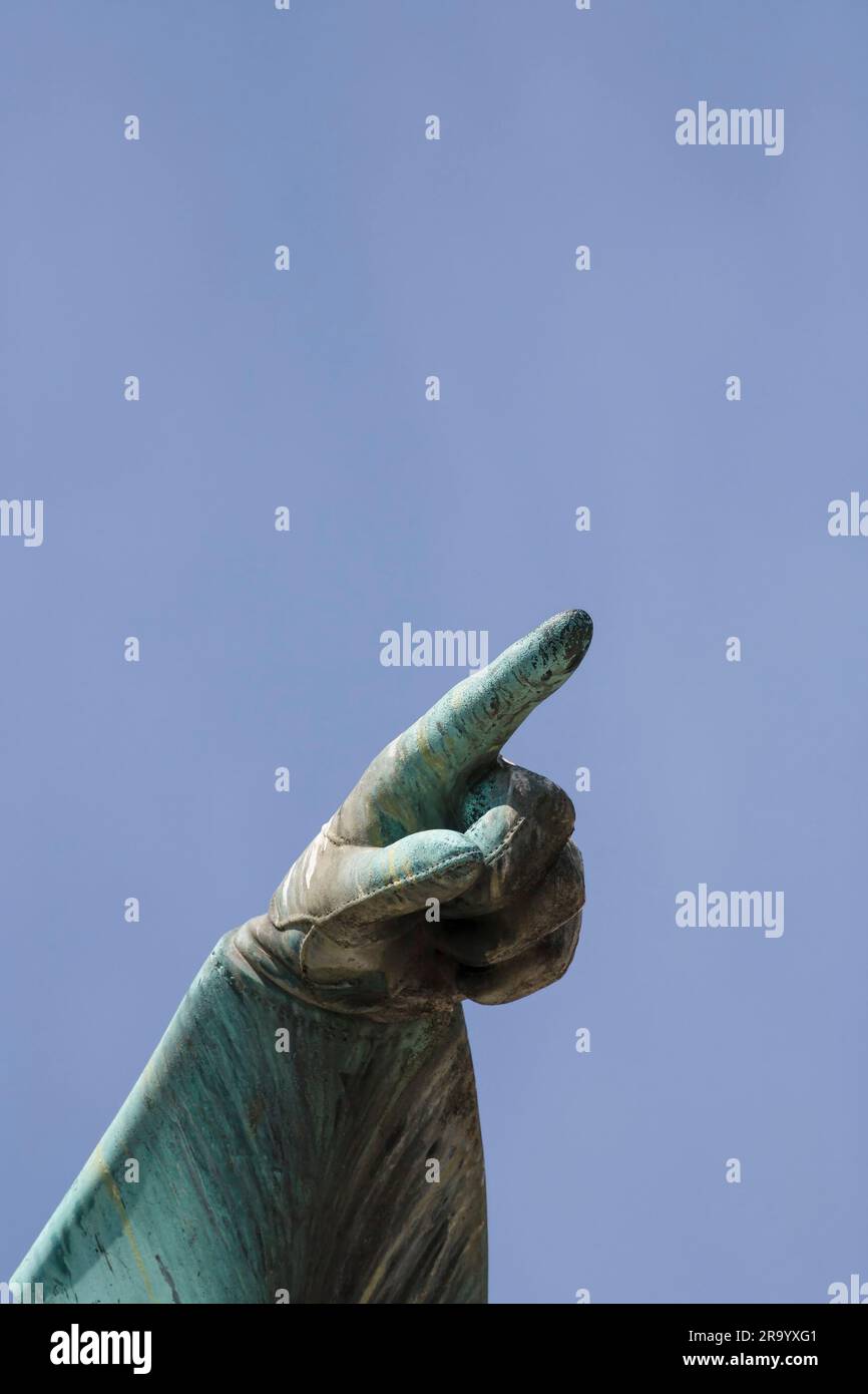 Close-up of hand pointing index finger against blue sky. Statue of Karl ...