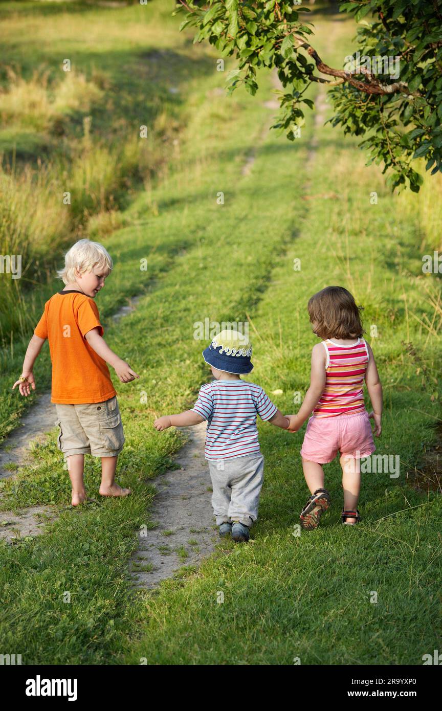 Rear view of children walking on grass below tree Stock Photo - Alamy