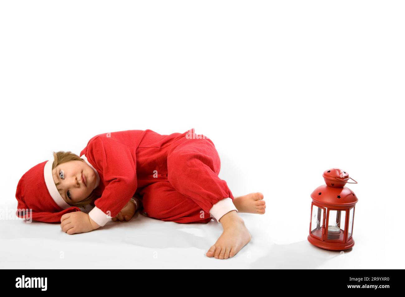 Santa girl resting on floor besides a red lantern over white background ...